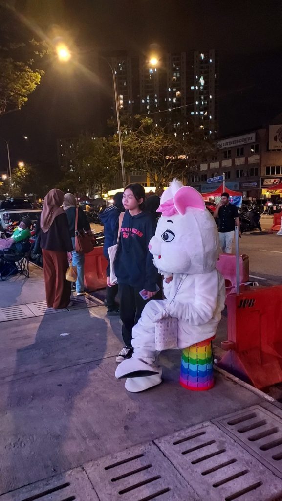 Elderly Lady Works As Mascot Cat At KL Bazaar, Gains Sympathy Of Passers-By